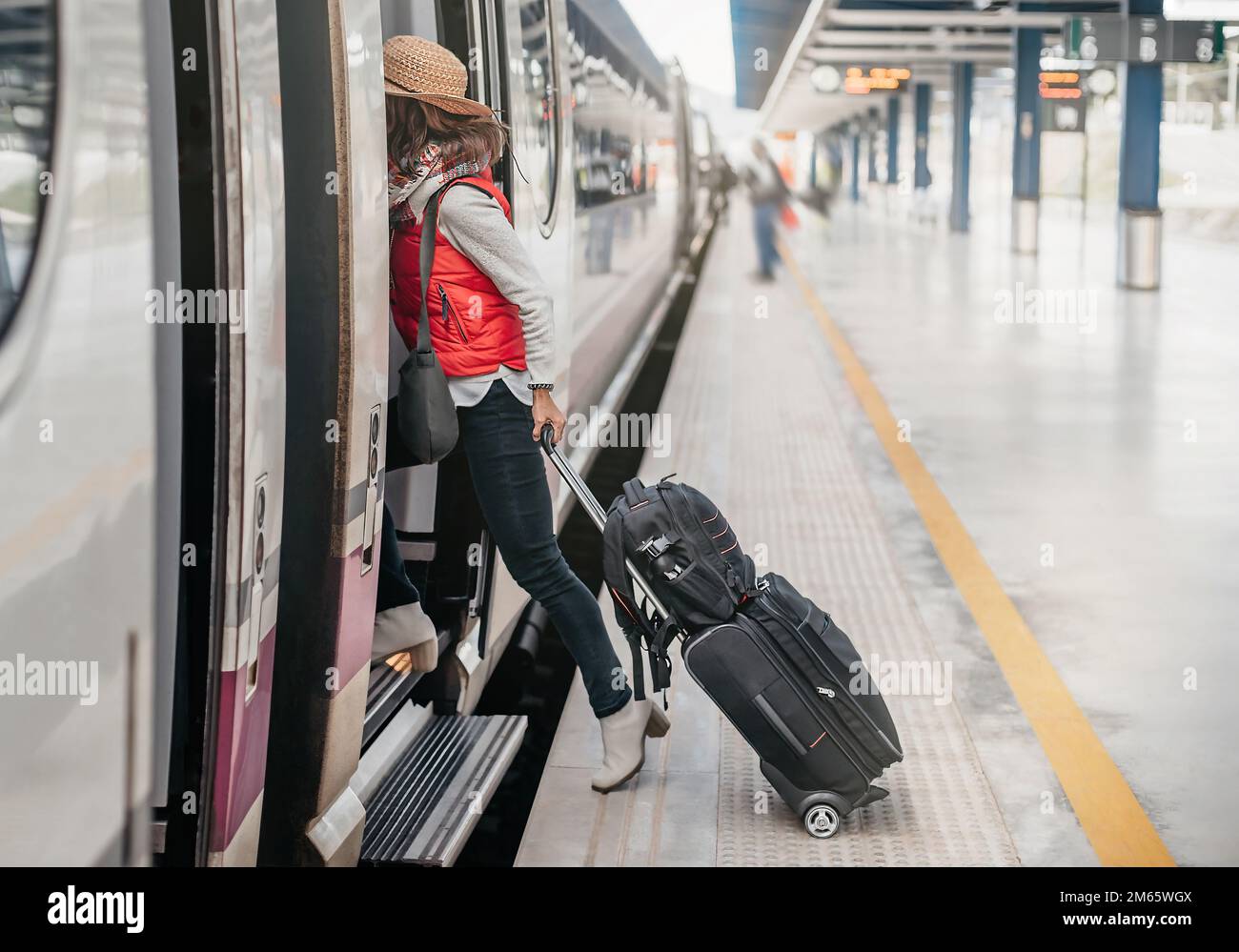 side view of a tourist with hand luggage, entering a train waiting at ...