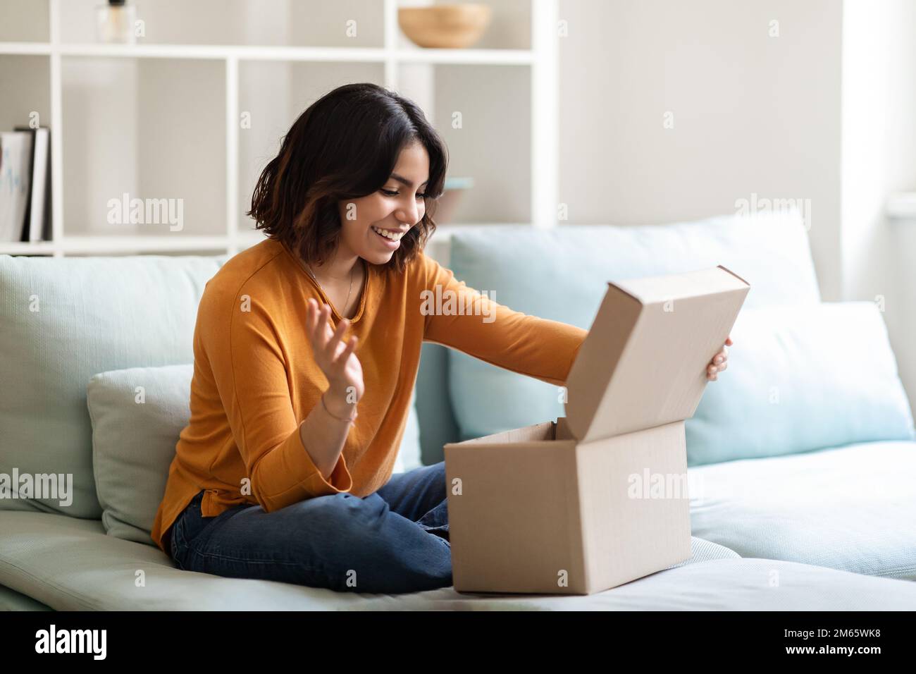 Happy young arab woman opening delivery box at home and looking inside ...