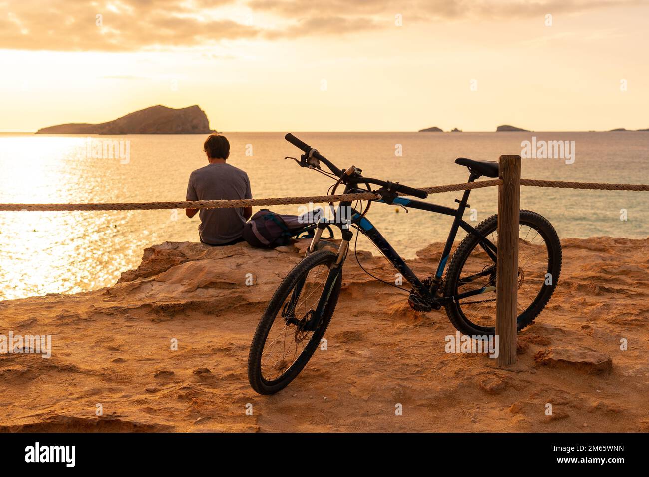 A tourist sitting on the edge of a cliff with his bike behind him on ...