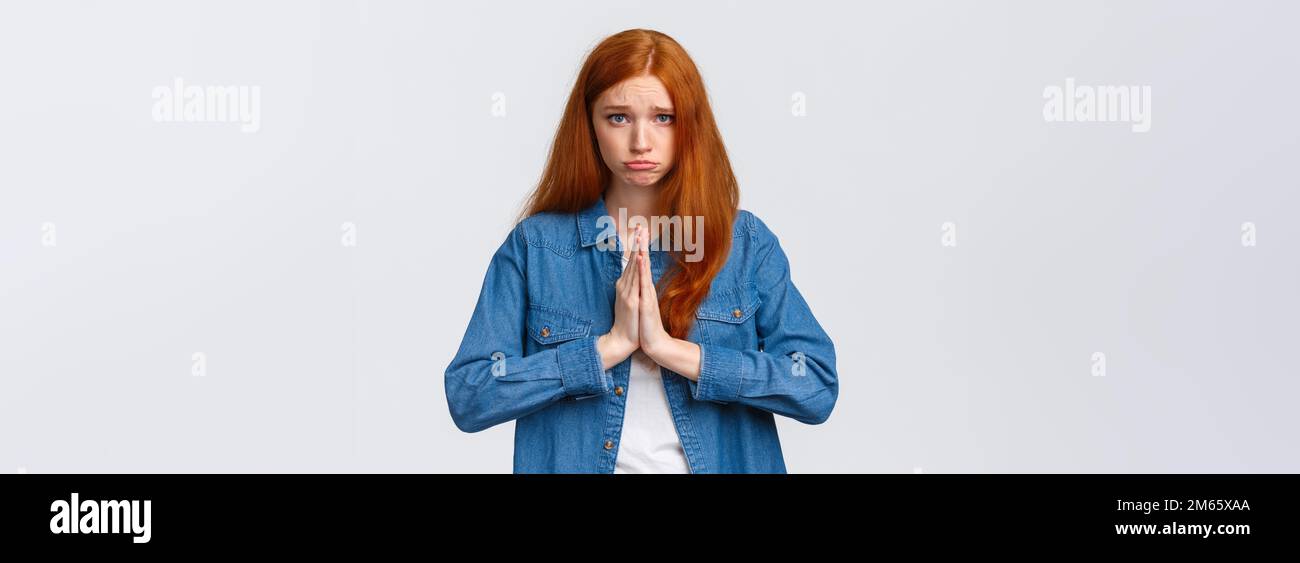 Waist-up portrait gloomy cute redhead girl begging aplogy, press hands together in pray, pouting ...