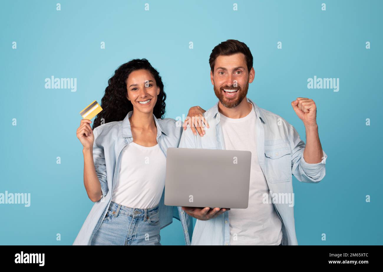 Smiling young european couple with credit card and laptop make gesture ...