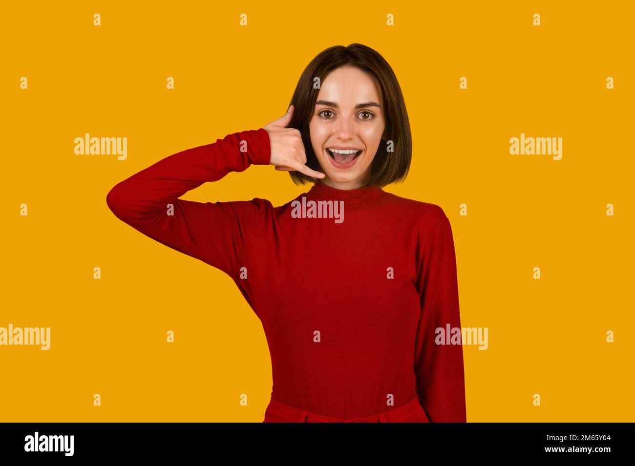 Friendly young woman showing call me sign and smiling Stock Photo - Alamy