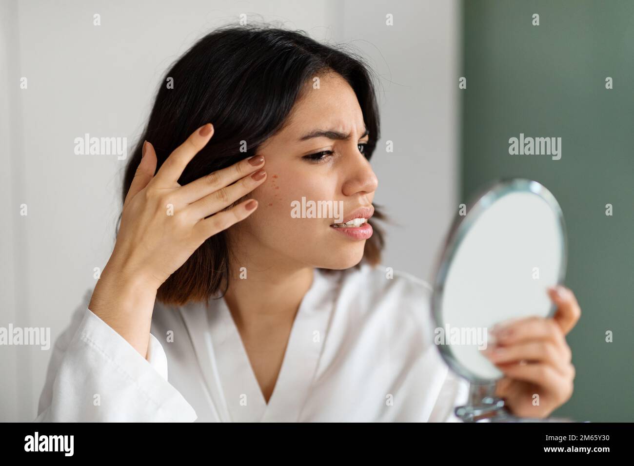 Sad young woman suffering from acne, checking skin in mirror Stock ...