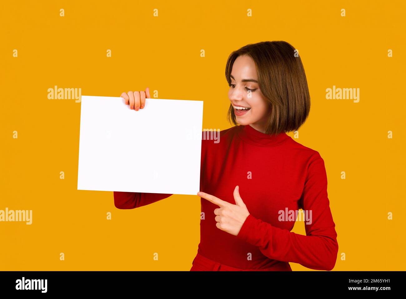 Happy beautiful young lady in red pointing at empty placard Stock Photo ...