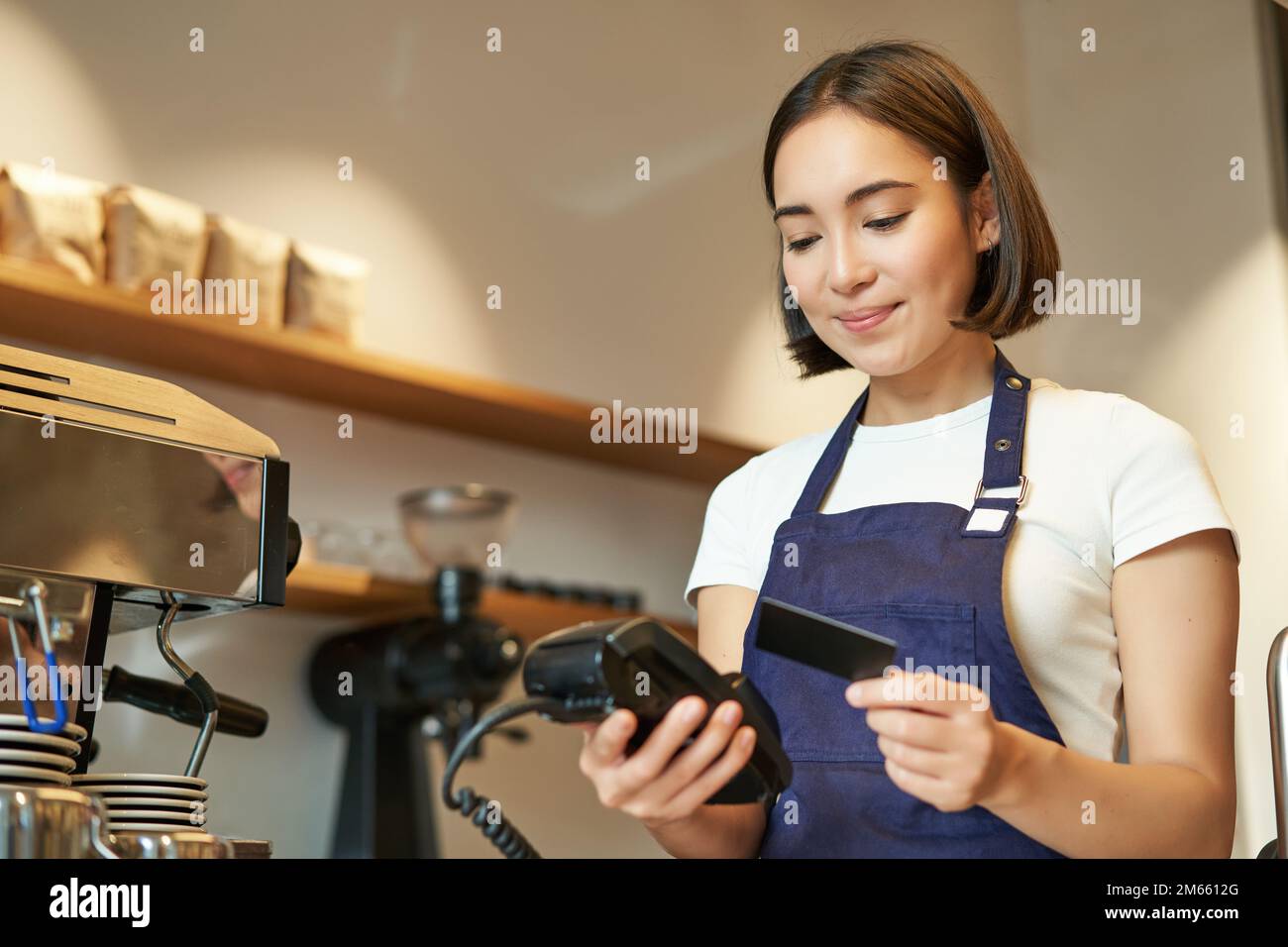 Cute asian girl, barista in cafe processing contactless payment, insert credit card into POS ...