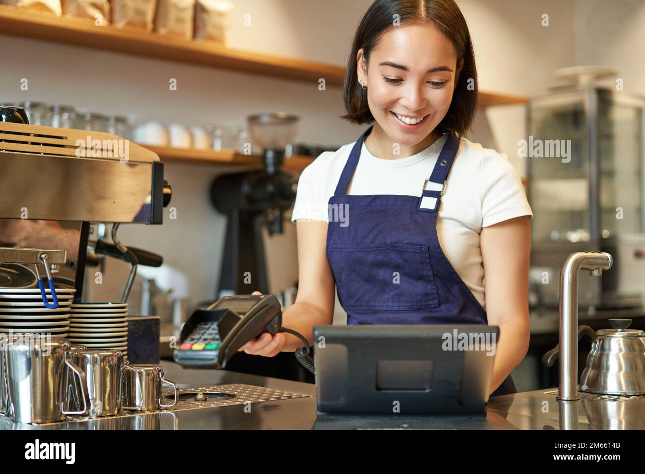 Smiling asian barista girl processing order, enter order in POS ...