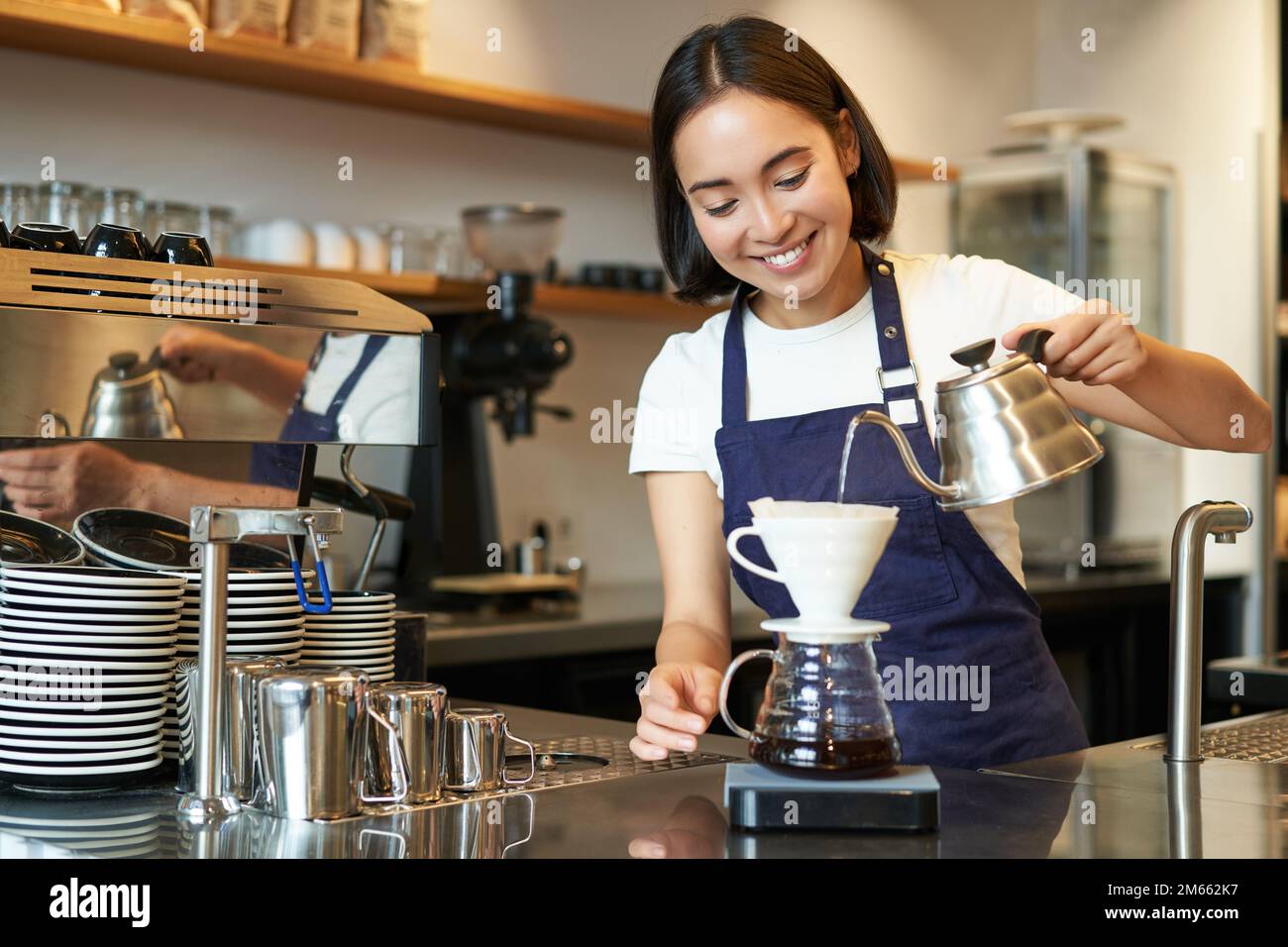 Cute brunette girl barista, cafe staff pouring water from kettle and ...