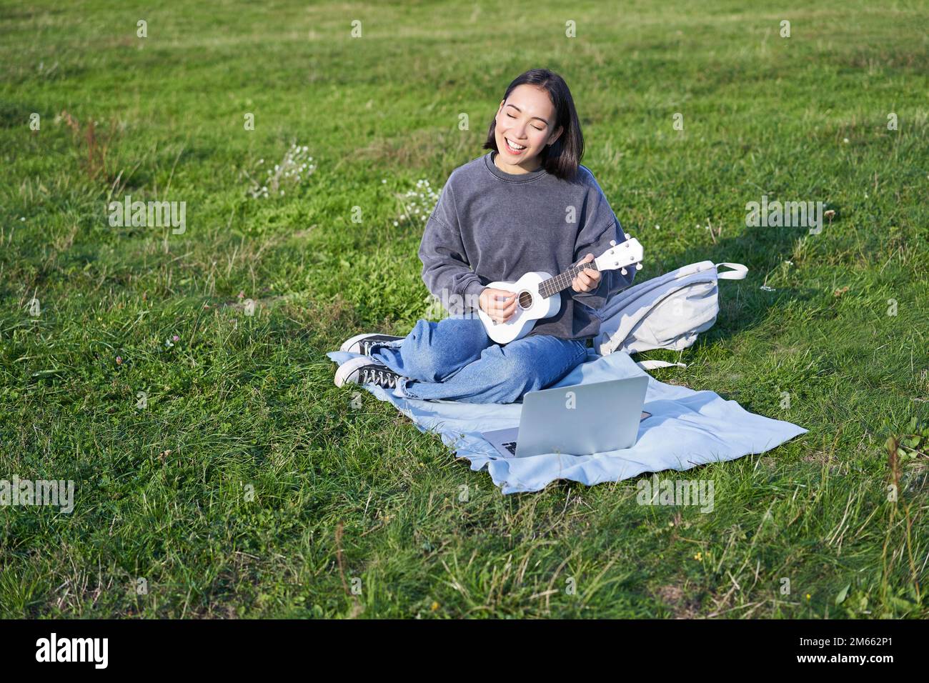 Cute korean girl, musician sits in park, plays ukulele and sings, looks ...