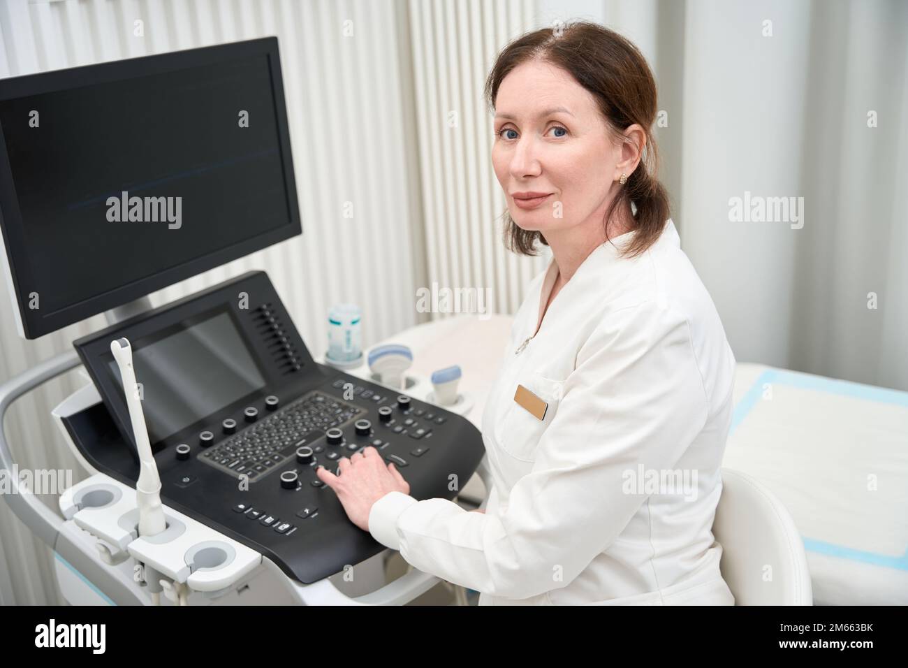 Middle-aged woman doctor sits at the workplace near ultrasound machine ...