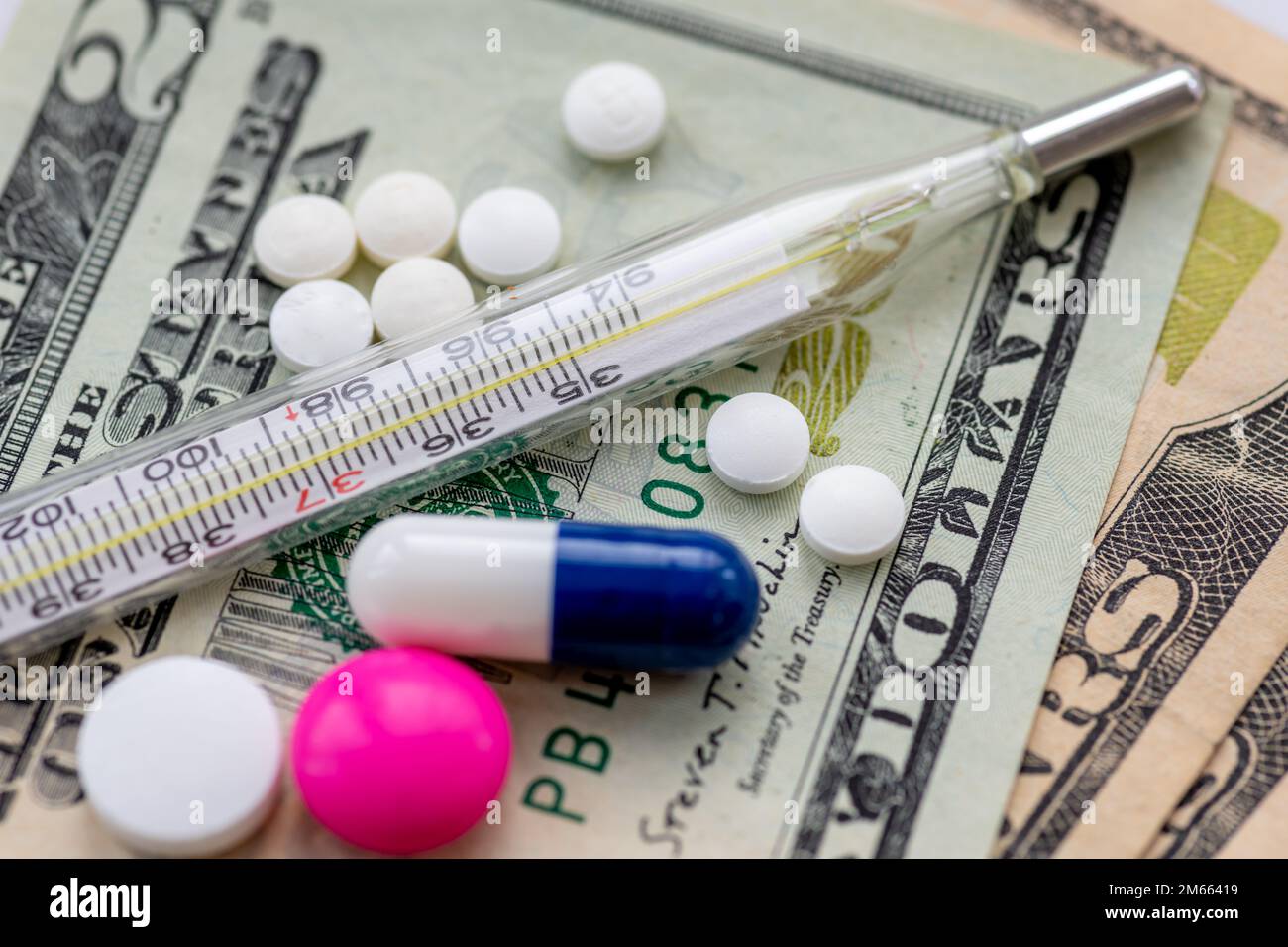Close up of medicine and a thermometer on top of Dollar bills. Heath ...