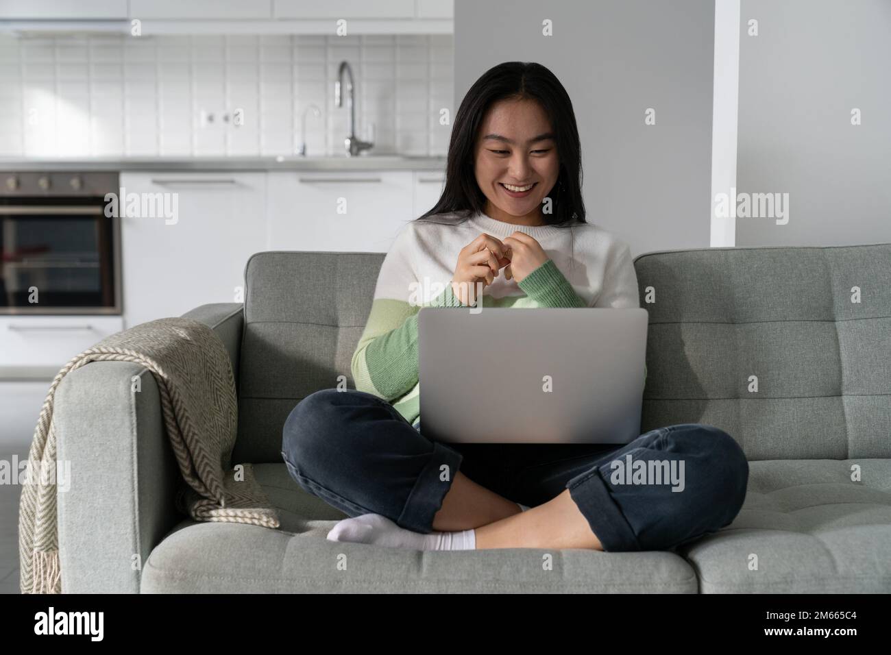 Happy smiling Asian girl sitting on sofa with laptop talking with ...