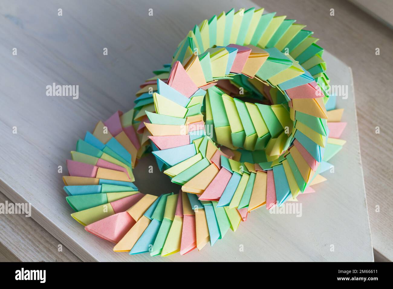Colorful origami rings lay on a white wooden table, abstract parametric ...
