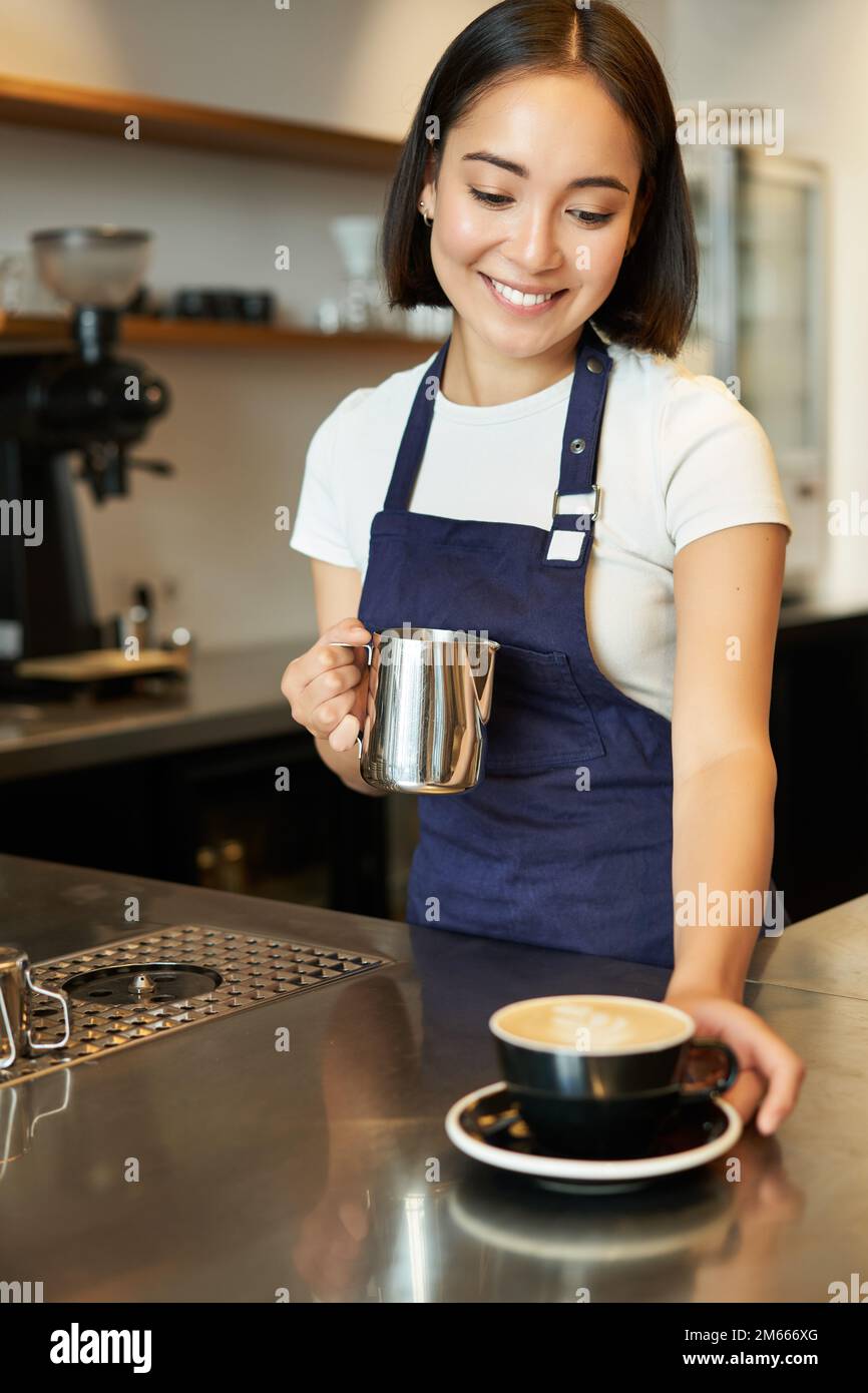 Vertical shot of smiling asian girl in cafe, giving out cappuccino ...