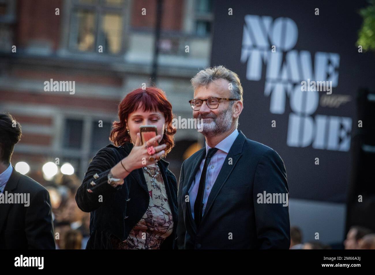 Hugh Dennis and his wife pose in front of the no time to die poster on ...