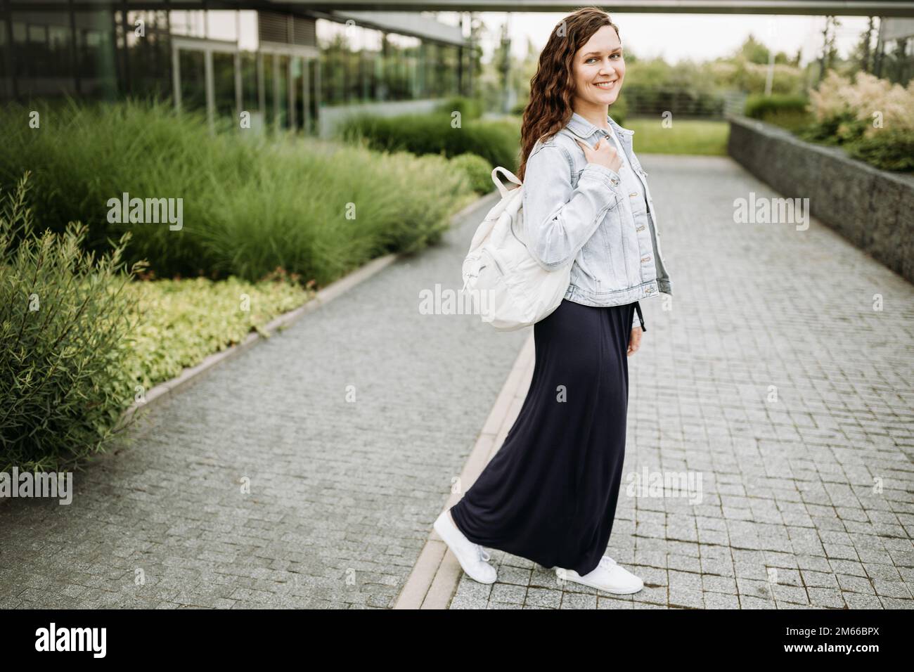 Happy pretty young brunette woman with white nylon backpack in blue ...