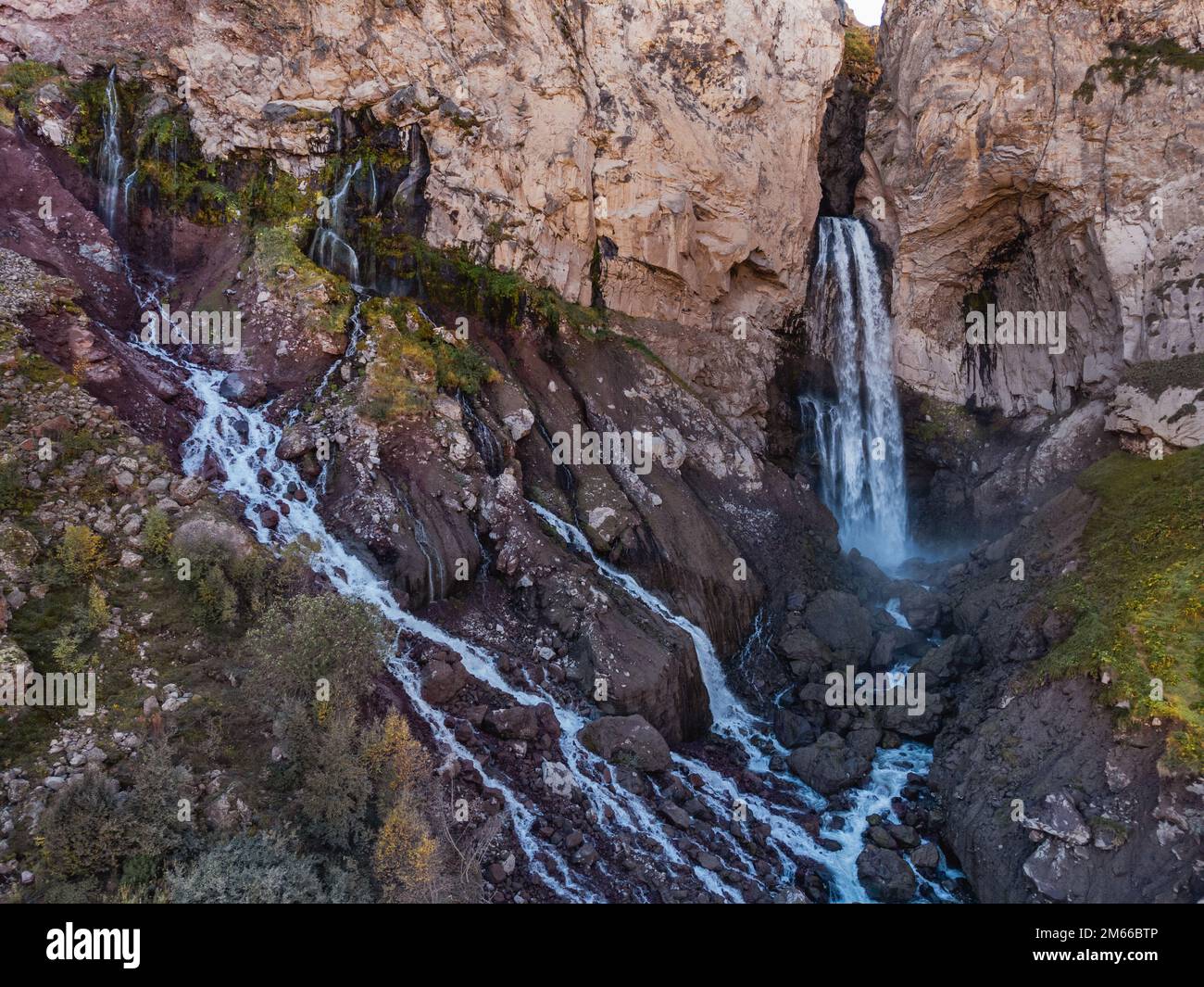 A smooth stream of water flows down from a cave in the high rocks of ...