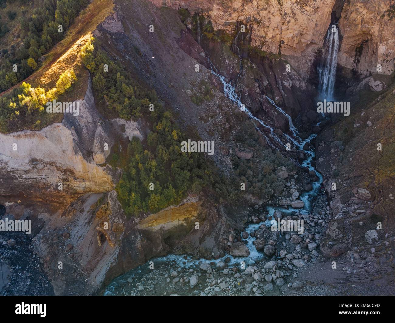 A smooth stream of water flows down from a cave in the high rocks of ...