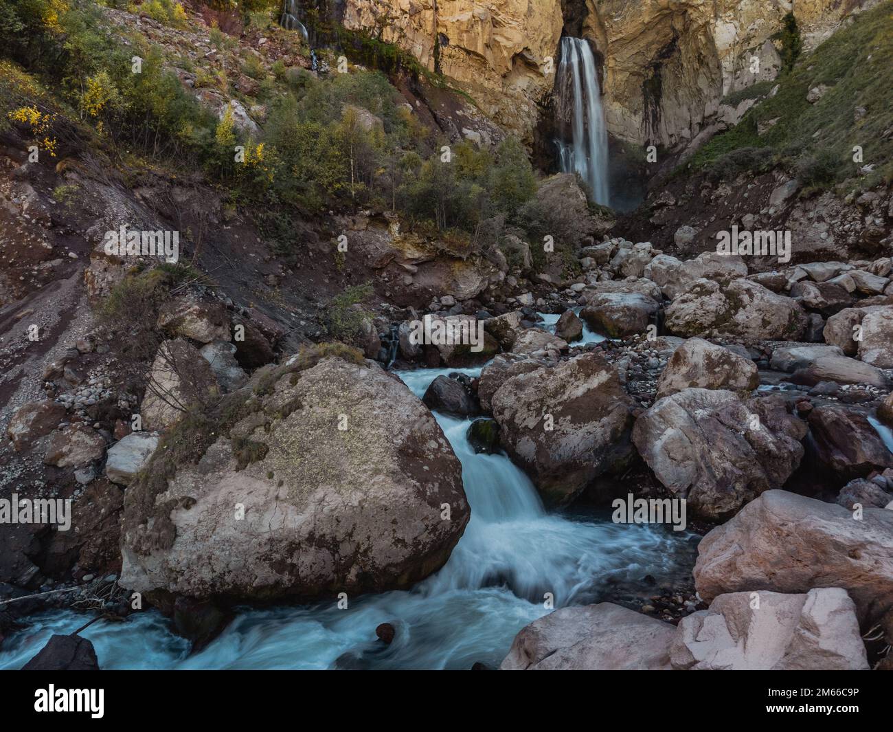 A smooth stream of water flows down from a cave in the high rocks of ...