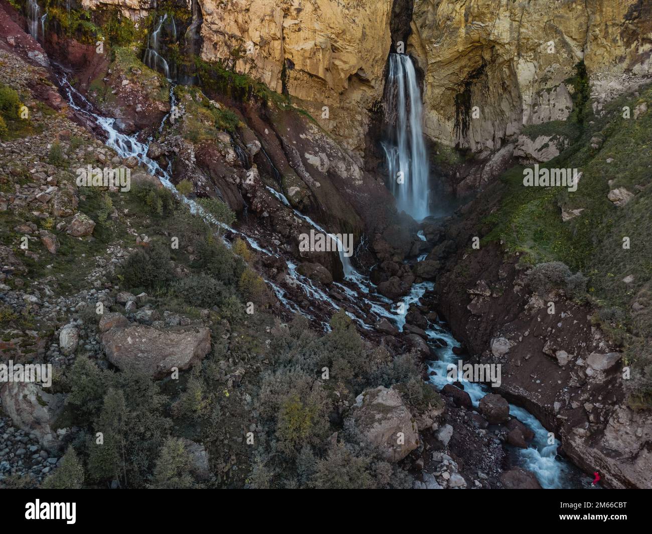 A smooth stream of water flows down from a cave in the high rocks of ...