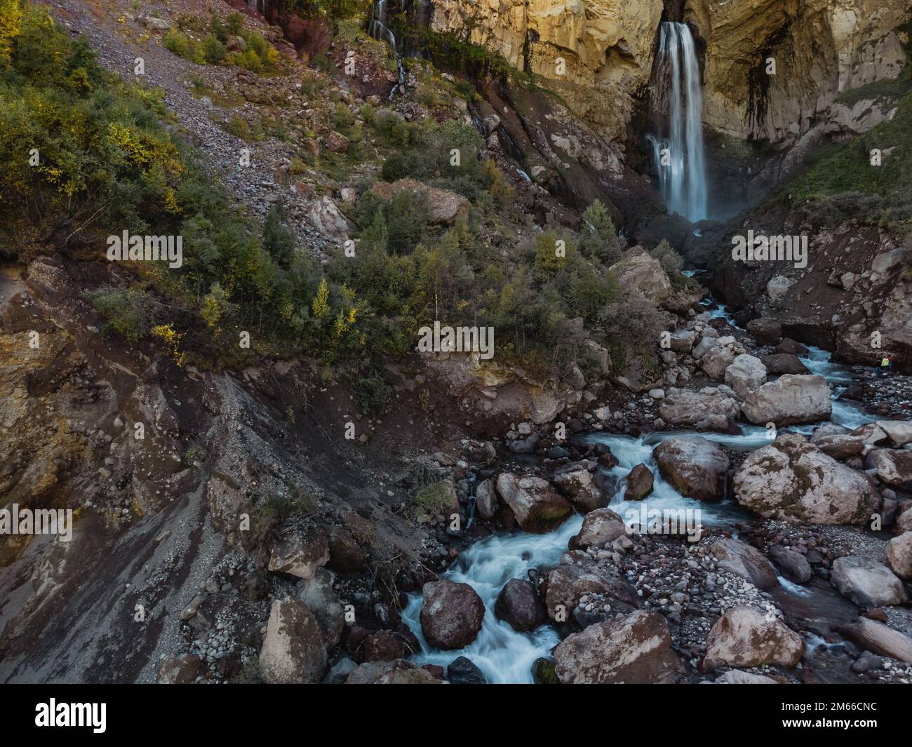 A smooth stream of water flows down from a cave in the high rocks of ...