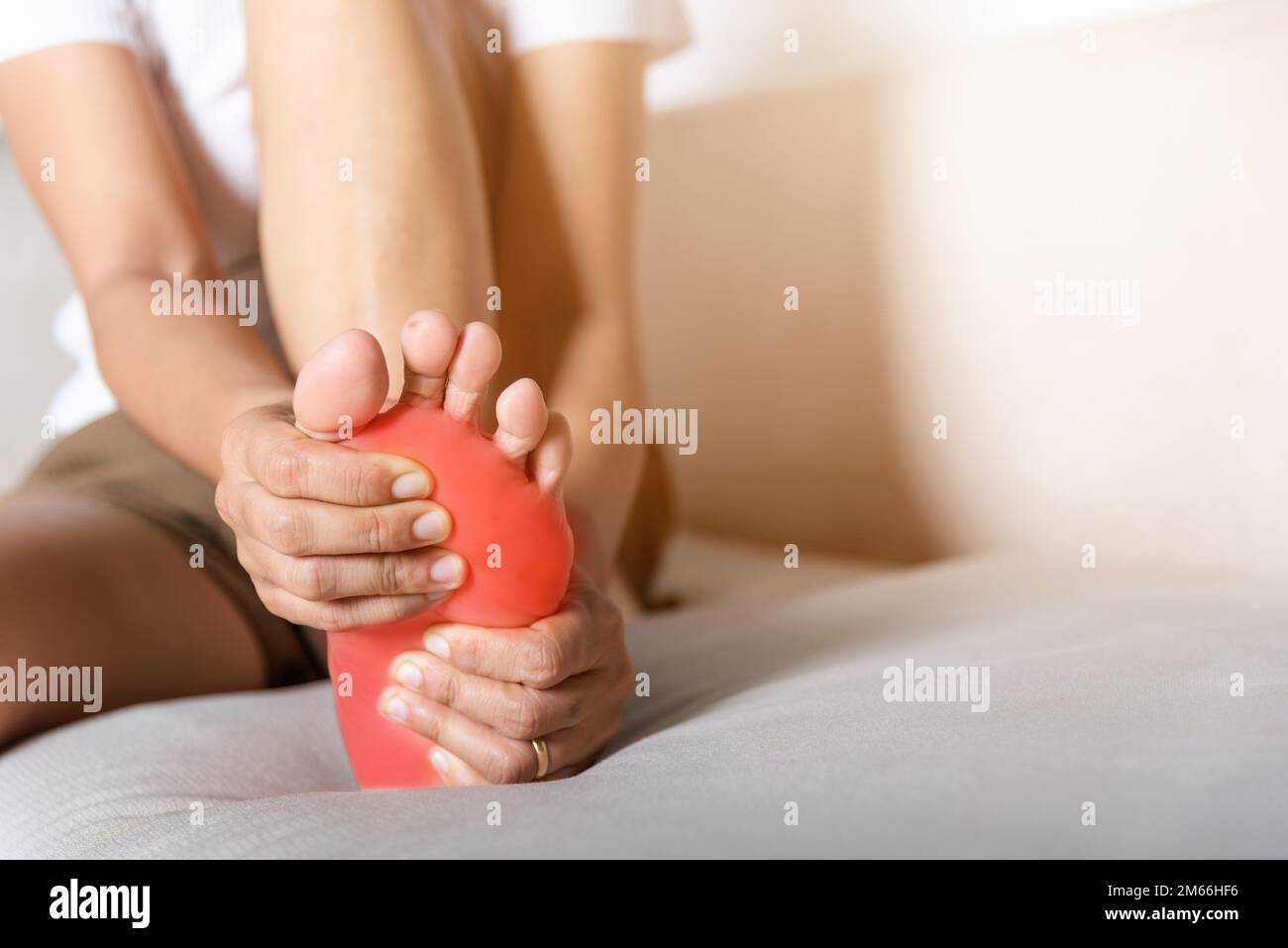Asian woman sitting on sofa feeling pain in her foot at home Stock ...