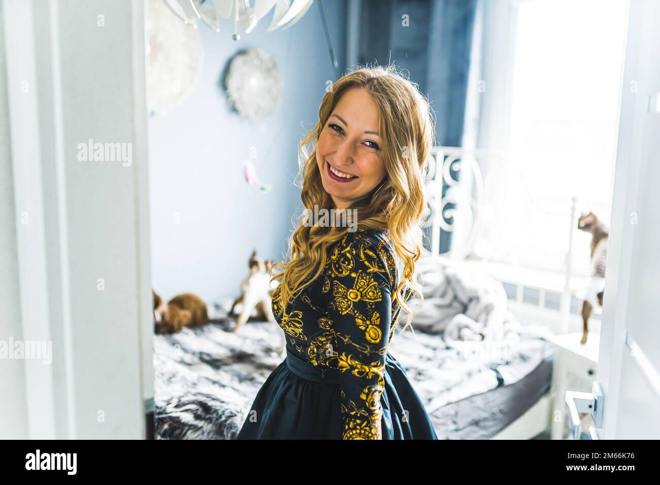 A picture with blonde woman smiling in the middle. Devon rex cats on the bed in the background ...