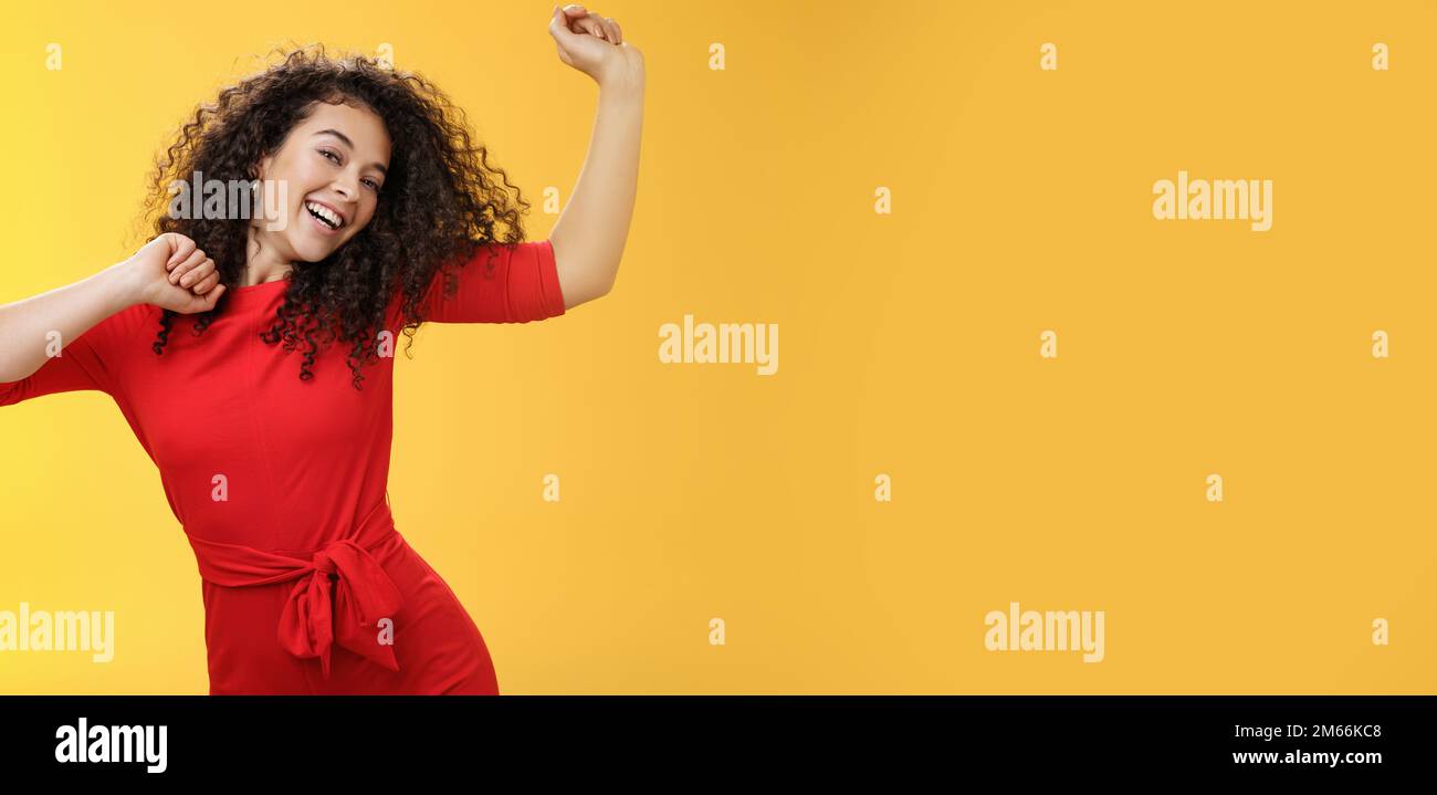 Carefree girl feeling uplifted and joyful dancing in red dress raising ...