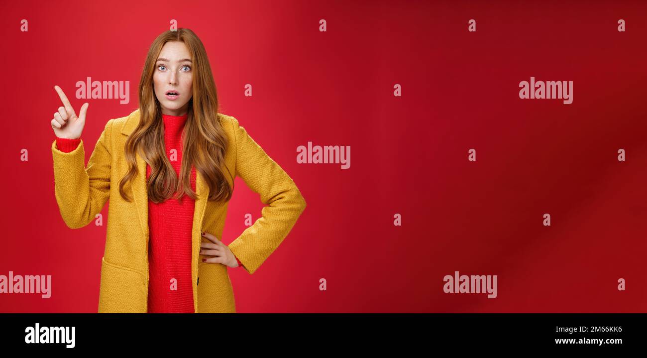 Shocked and stunned cute, confused ginger girl in yellow coat feeling ...