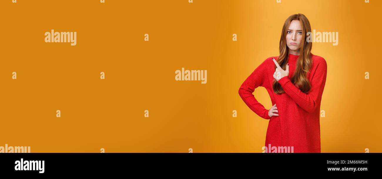 Upset and disappointed young ginger girl in red sweater pointing at ...