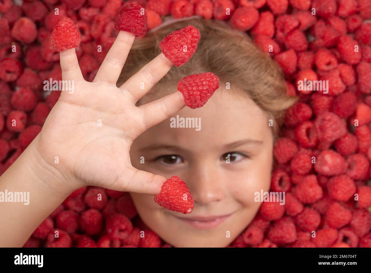 Top view photo of child face in raspberries background. Healthy eating ...