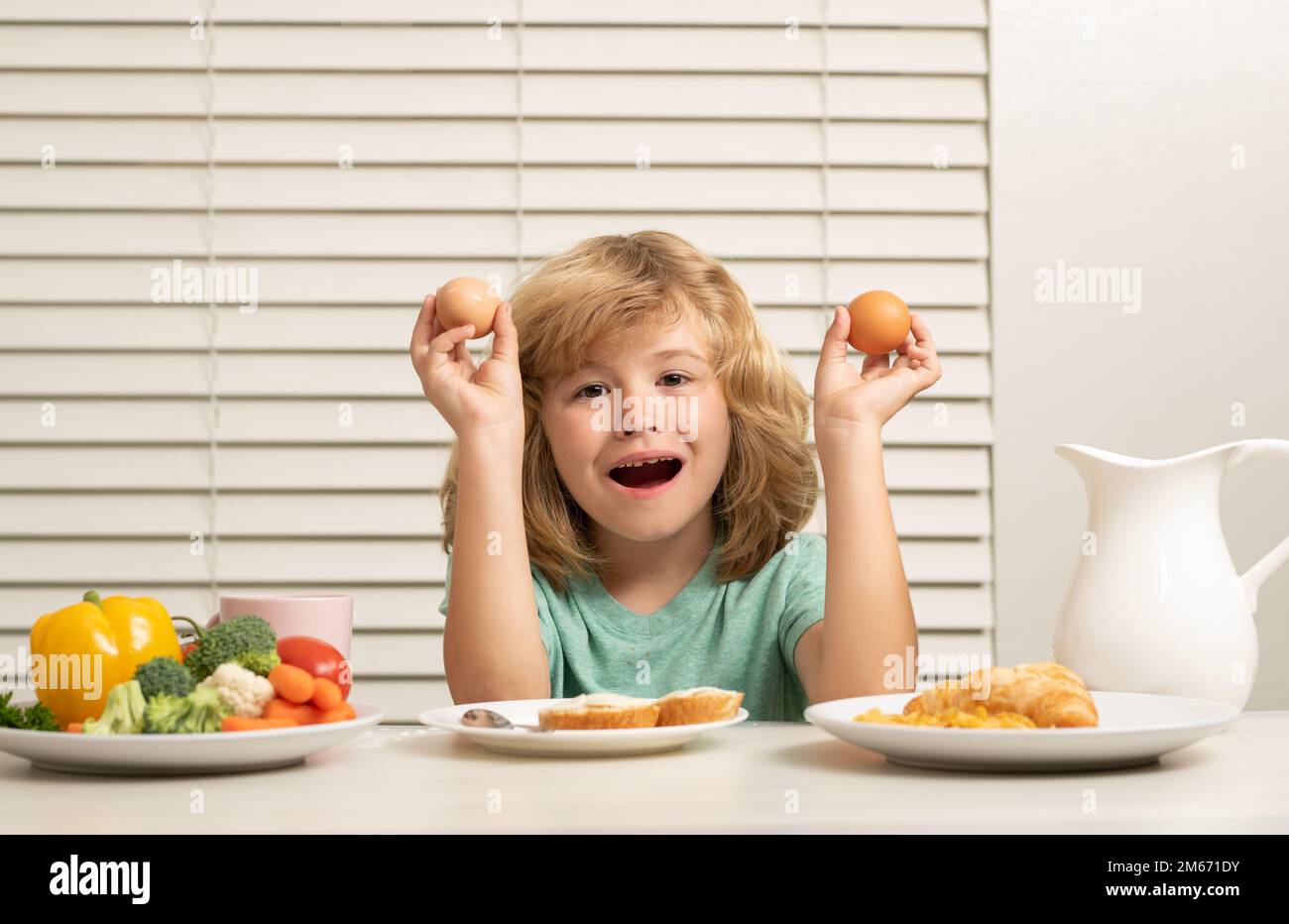 Kid eating egg. Child in the kitchen at the table eating vegetable and ...