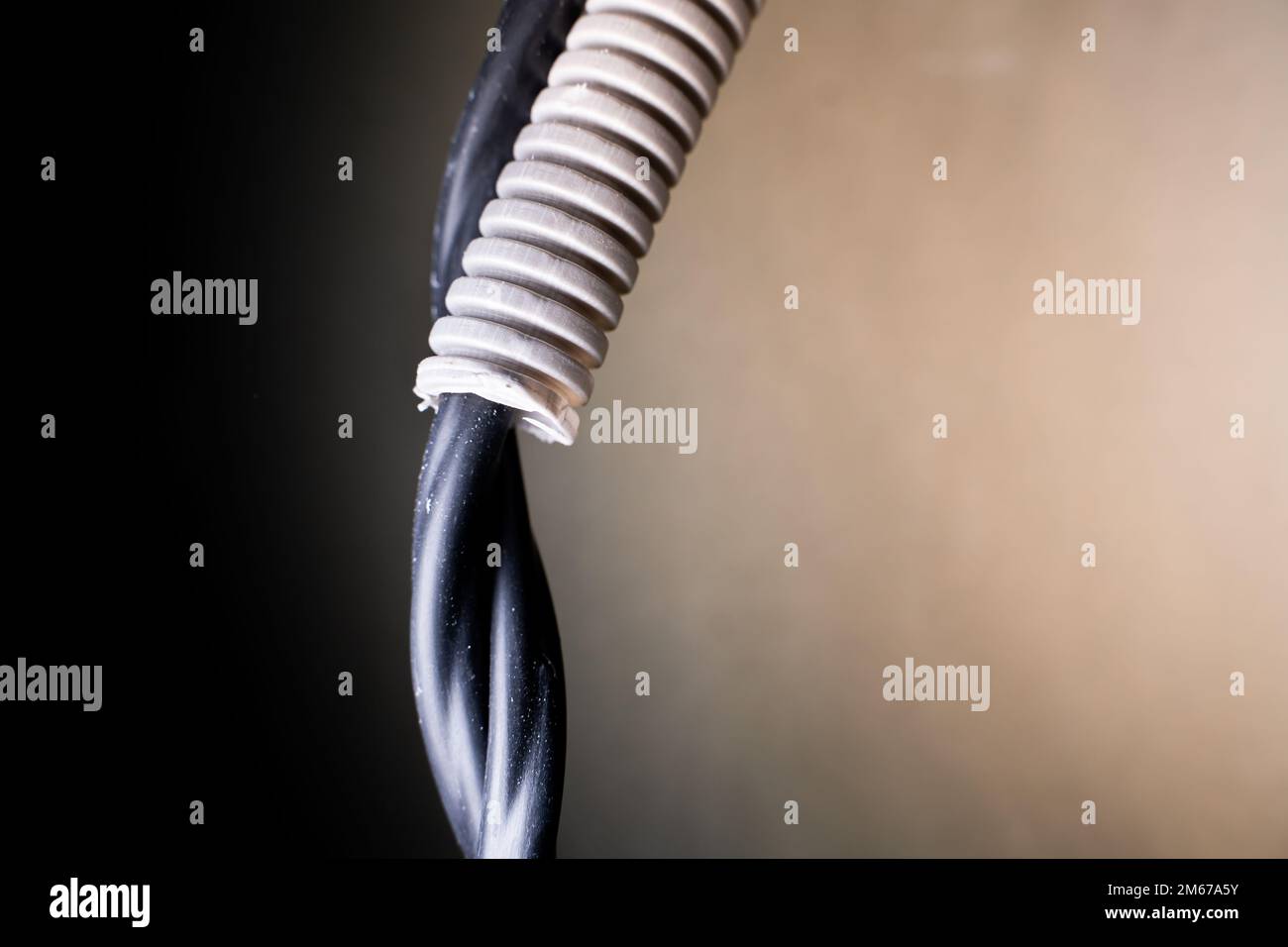 A black power wire enters a plastic gray corrugated tube close-up on a ...