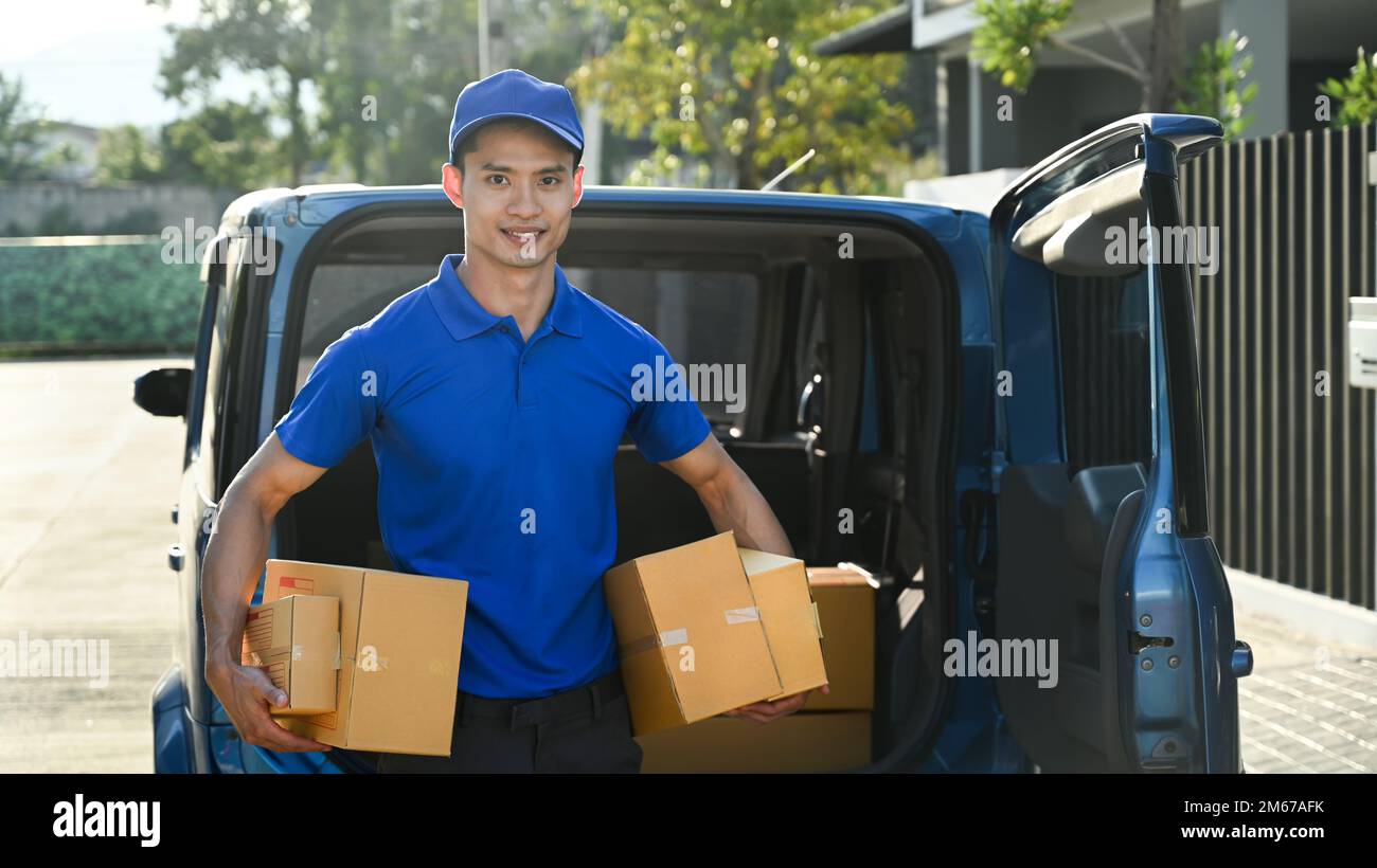 Portrait of delivery man wearing blue uniform with cardboard in hands ...