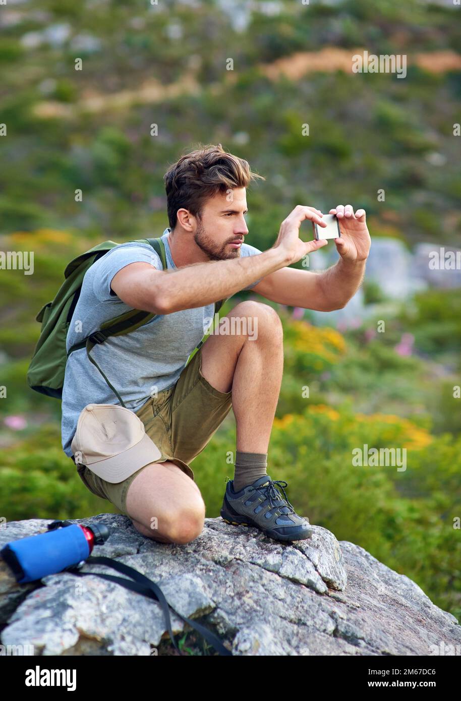 Capturing the view. a handsome young man snapping pics while hiking ...