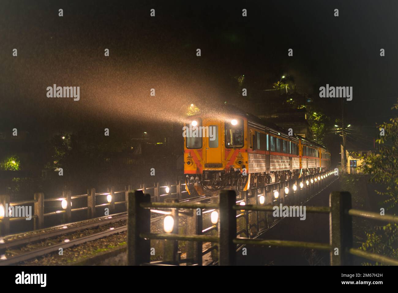 The train with lights on was running on the bridge in the rain ...