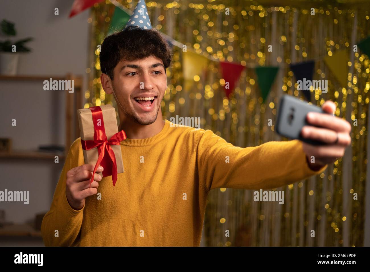 Young happy man holding gift box with red ribbon using mobile phone for ...