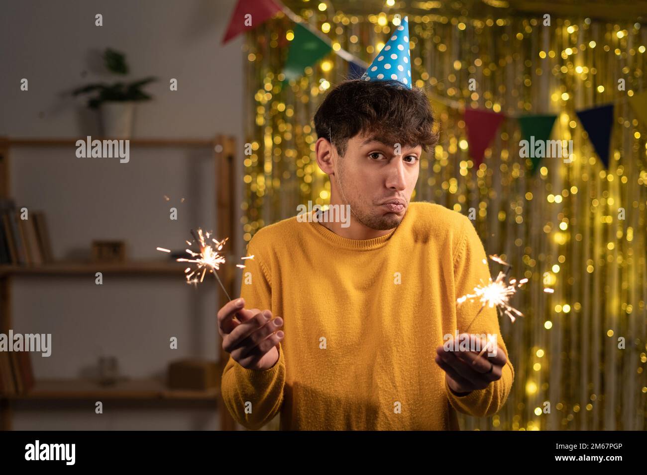 Young man wearing birthday party hat surprised and shocked, looking ...