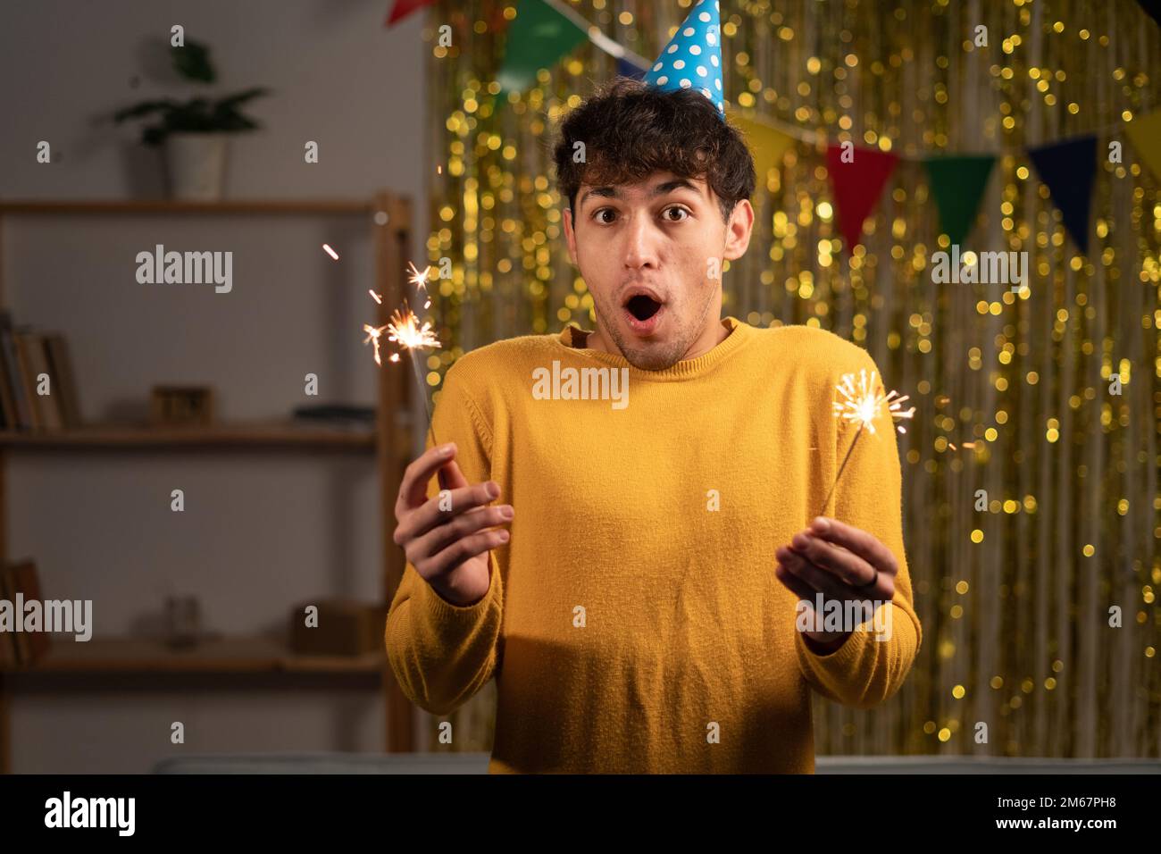 Surprised guy celebrating birthday at home with sparklers stands with ...