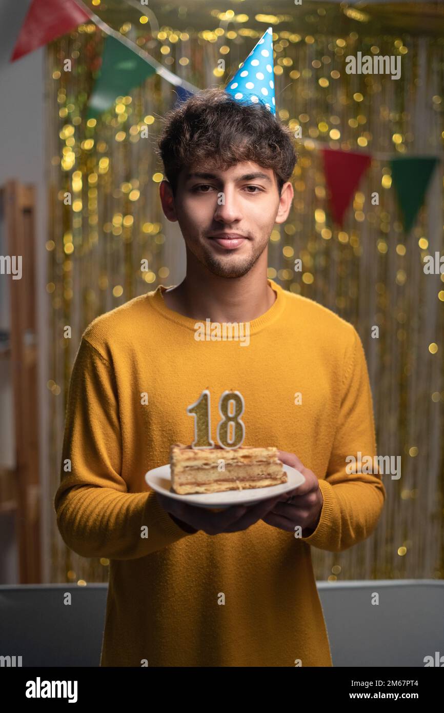 18th birthday. Young arabic man in party hat holding cake with number ...