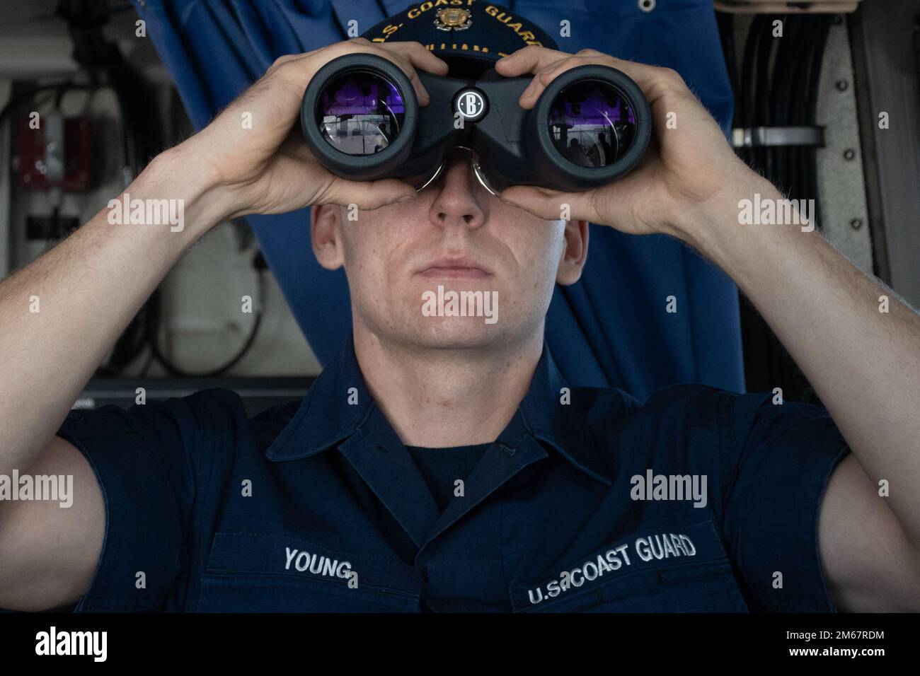 Coast Guard Seaman Holden Young uses binoculars as he surveys the ...