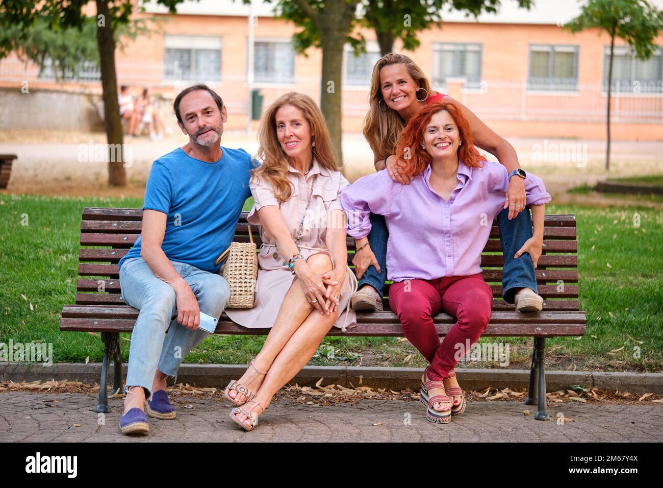 Four mature adults looking at camera sitting on a bench in a park Stock ...