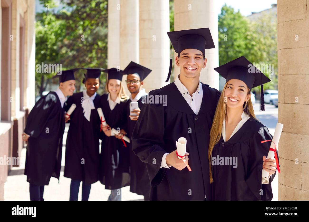 Happy couple students in graduation dresses and hats enjoy graduation ...
