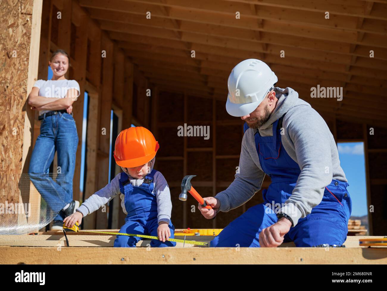 Father, mother and son building wooden frame house. Toddler boy helping ...