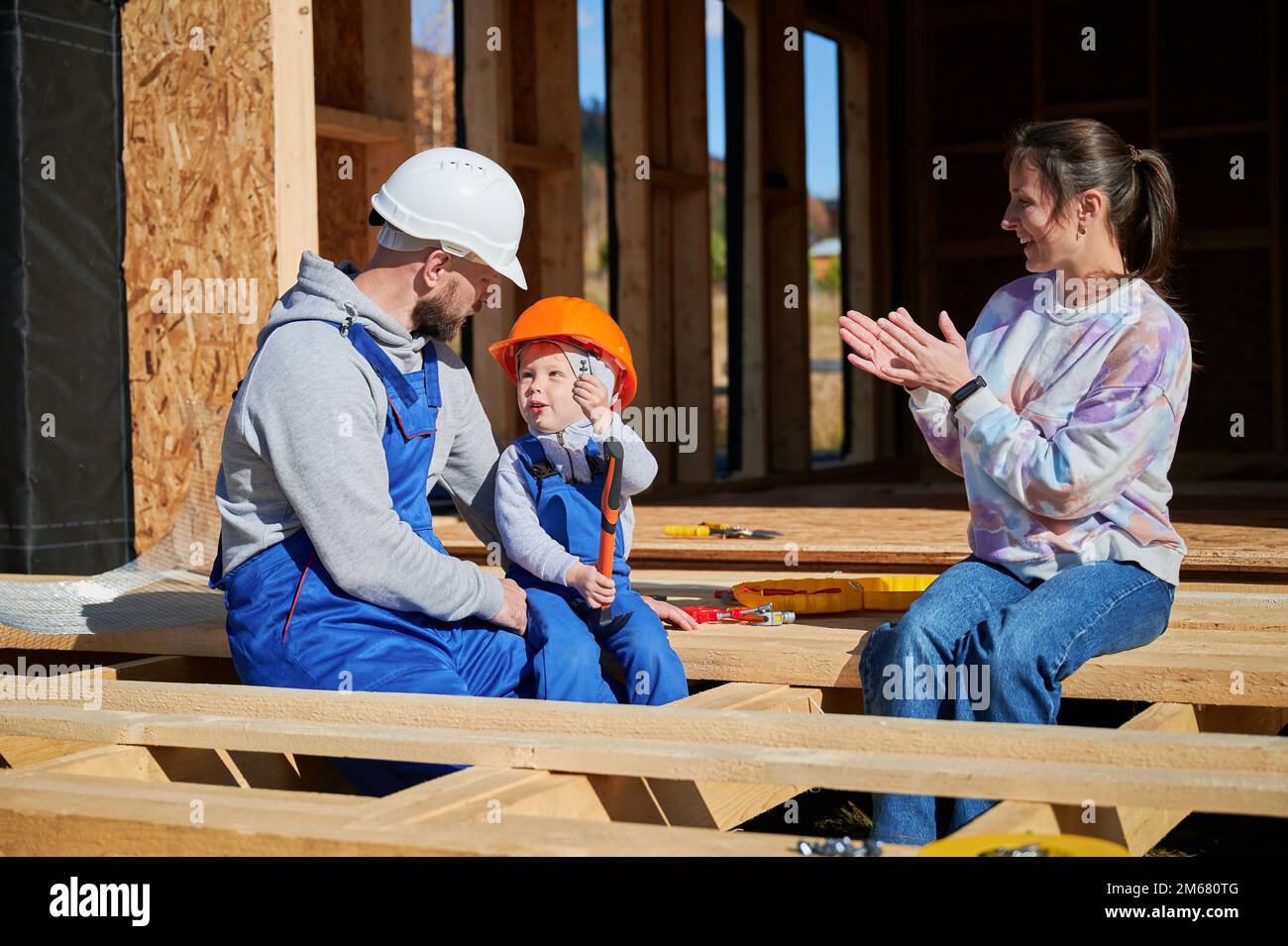 Father, mother and son building wooden frame house. Toddler boy helping ...