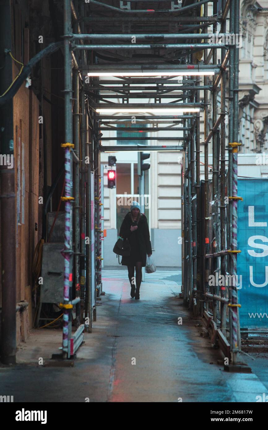 A pedestrian walks through scaffolding on a sidewalk, lit with neon ...