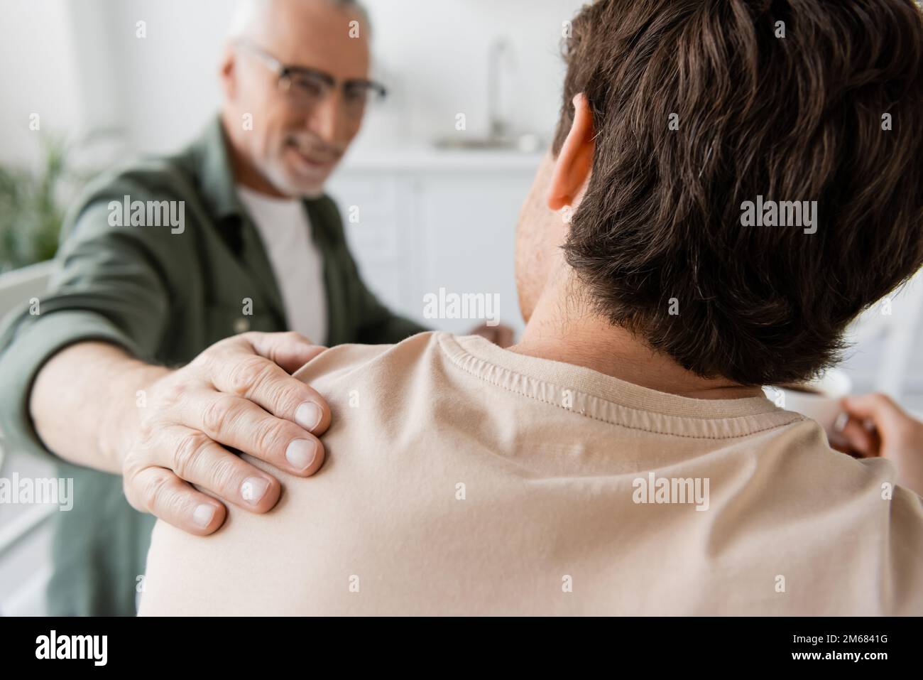 blurred senior man touching shoulder of young son in kitchen,stock ...