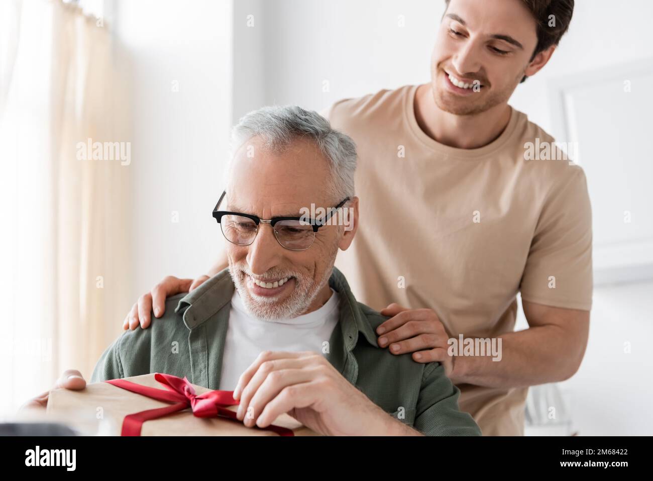 smiling man touching shoulders of happy dad opening fathers day present ...