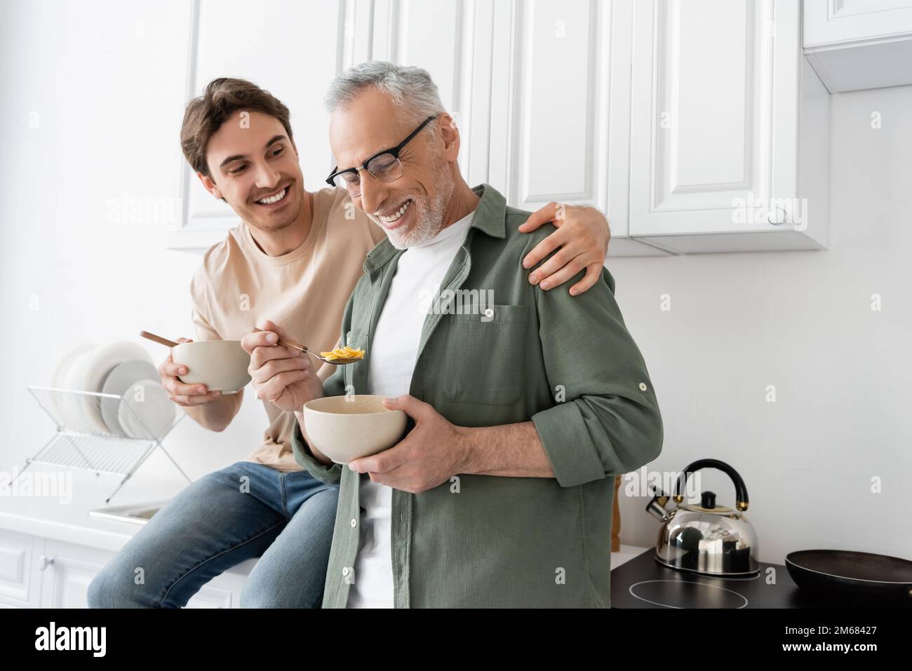 happy young man sitting on kitchen worktop and hugging shoulders of ...