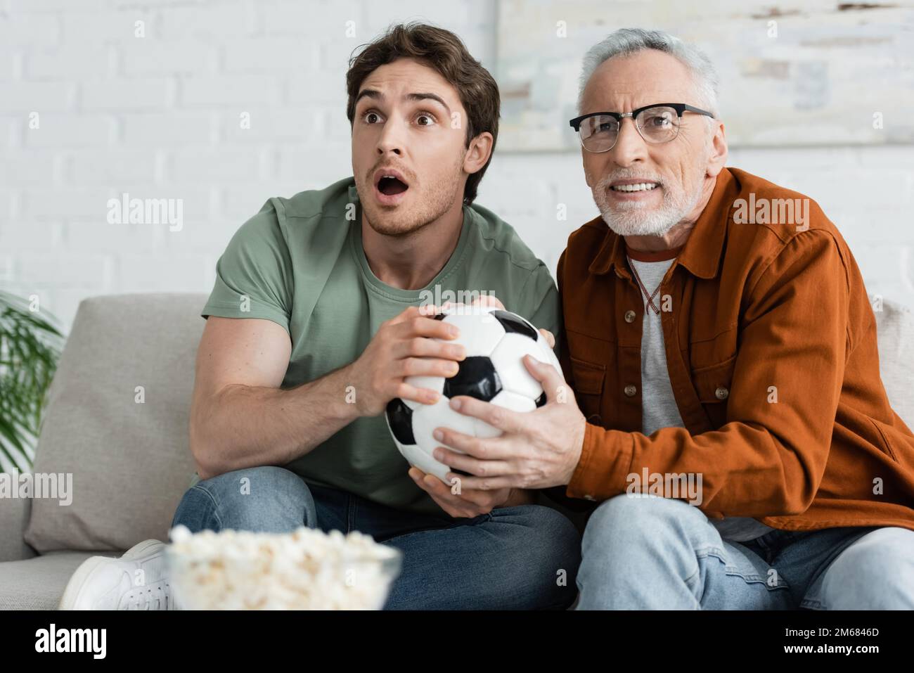thrilled guy with tense dad holding soccer ball while watching football ...