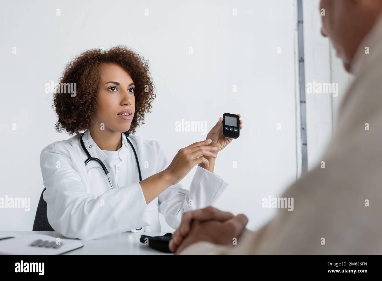 curly african american doctor holding glucose meter device near middle ...